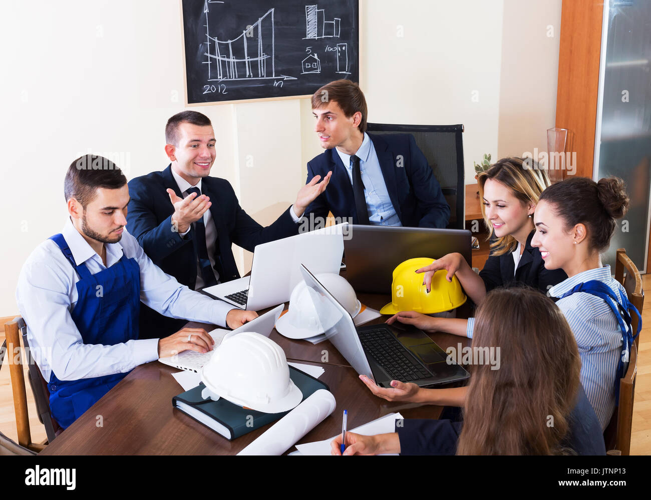 Team of young positive professionals with helmets and laptops on the ...