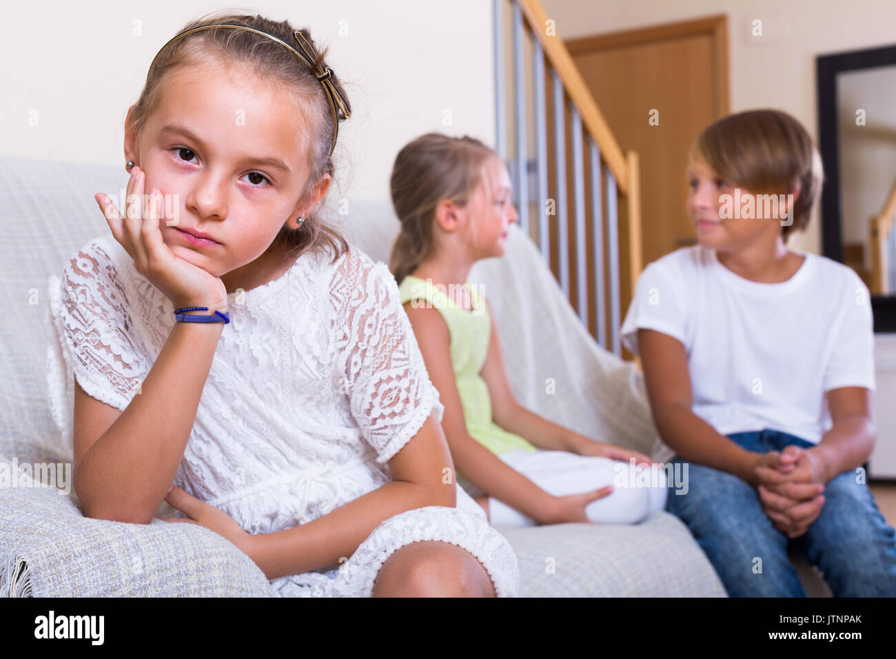 Envy girl sitting aside of couple children at home Stock Photo - Alamy