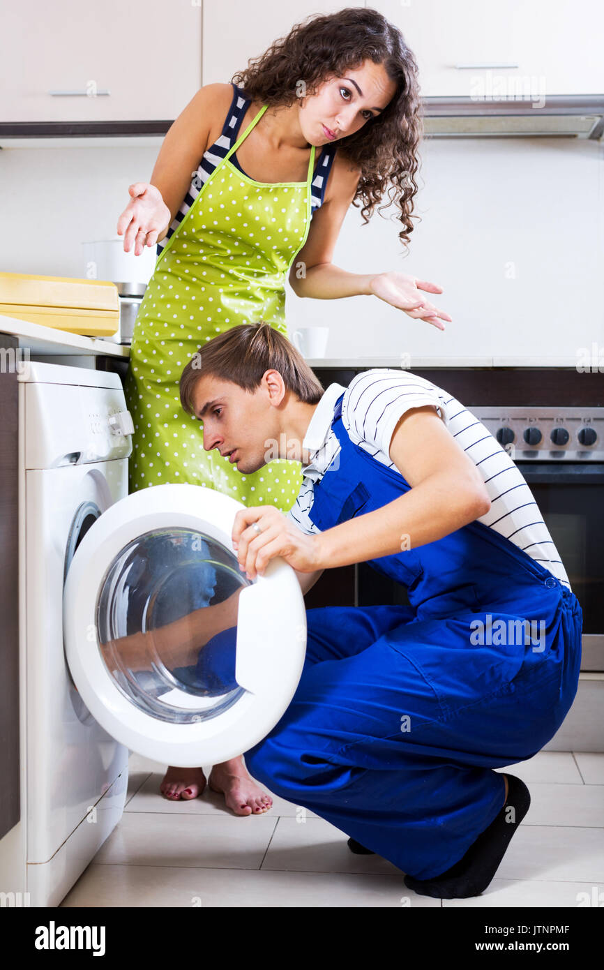 Young serviceman and sad woman standing near washing machine indoors ...