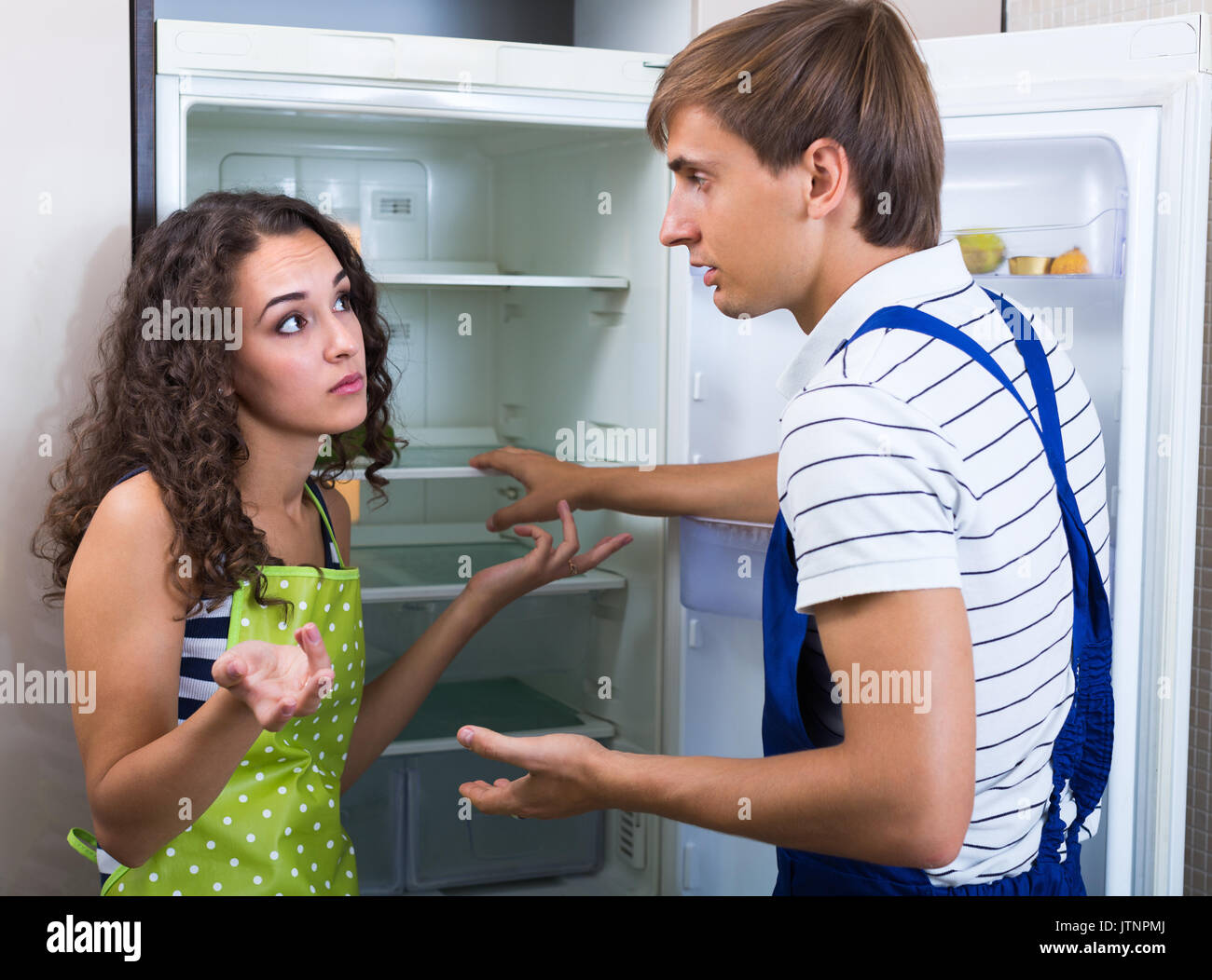 Tired handyman cannot repair refrigerator at the kitchen of female ...