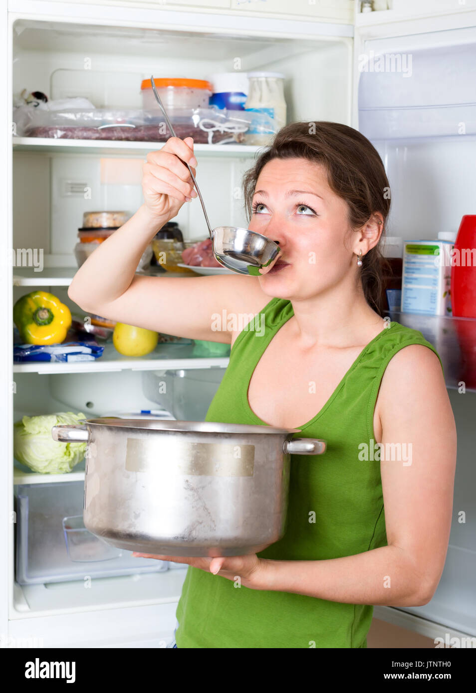 Famished woman eating from a stainless steel pan with a soup laddle ...