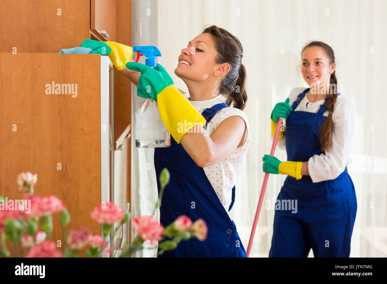 Two smiling young women in uniform cleaning in the house with rags and ...
