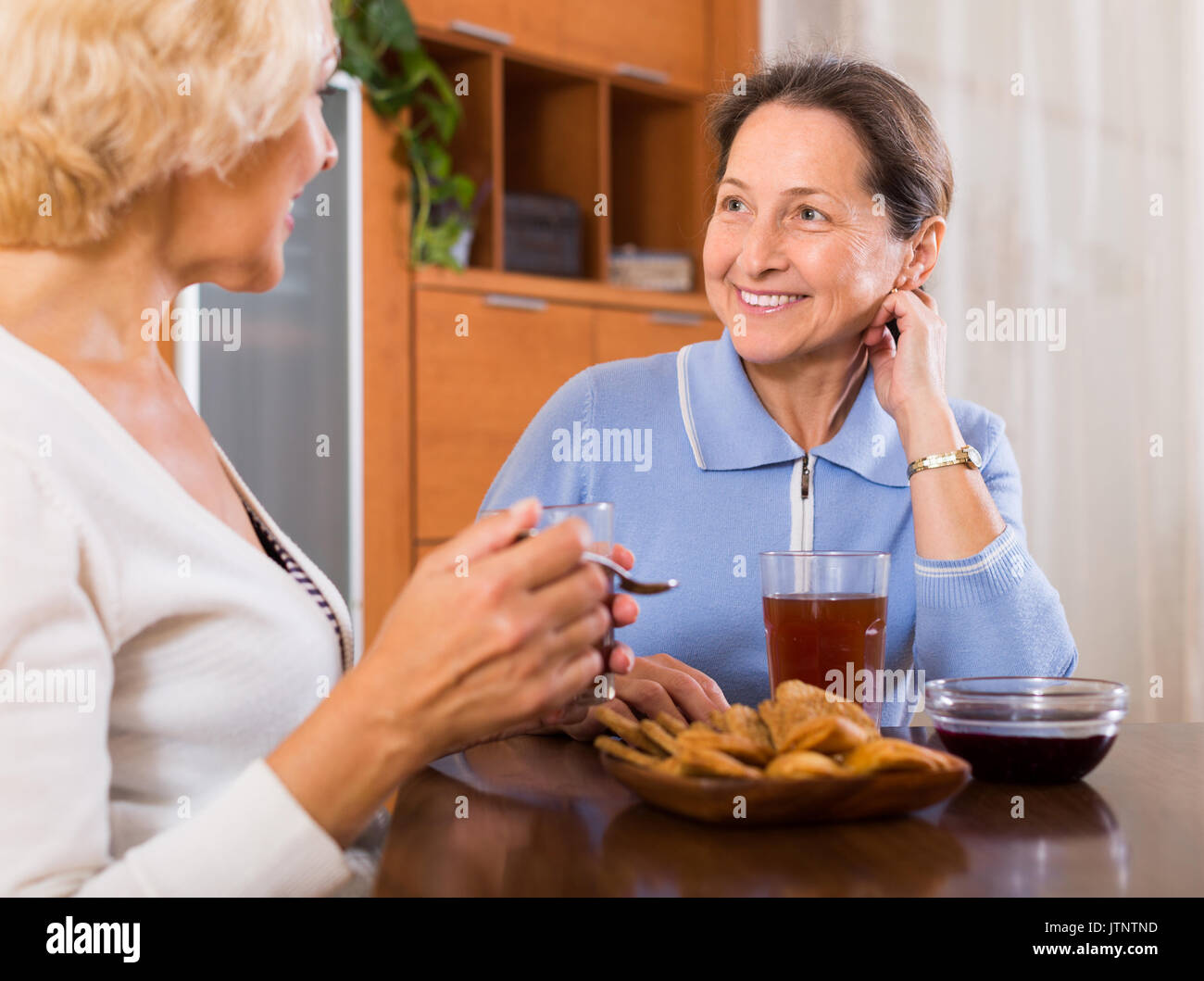 Two smiling positive female pensioners drinking tea at the table at ...