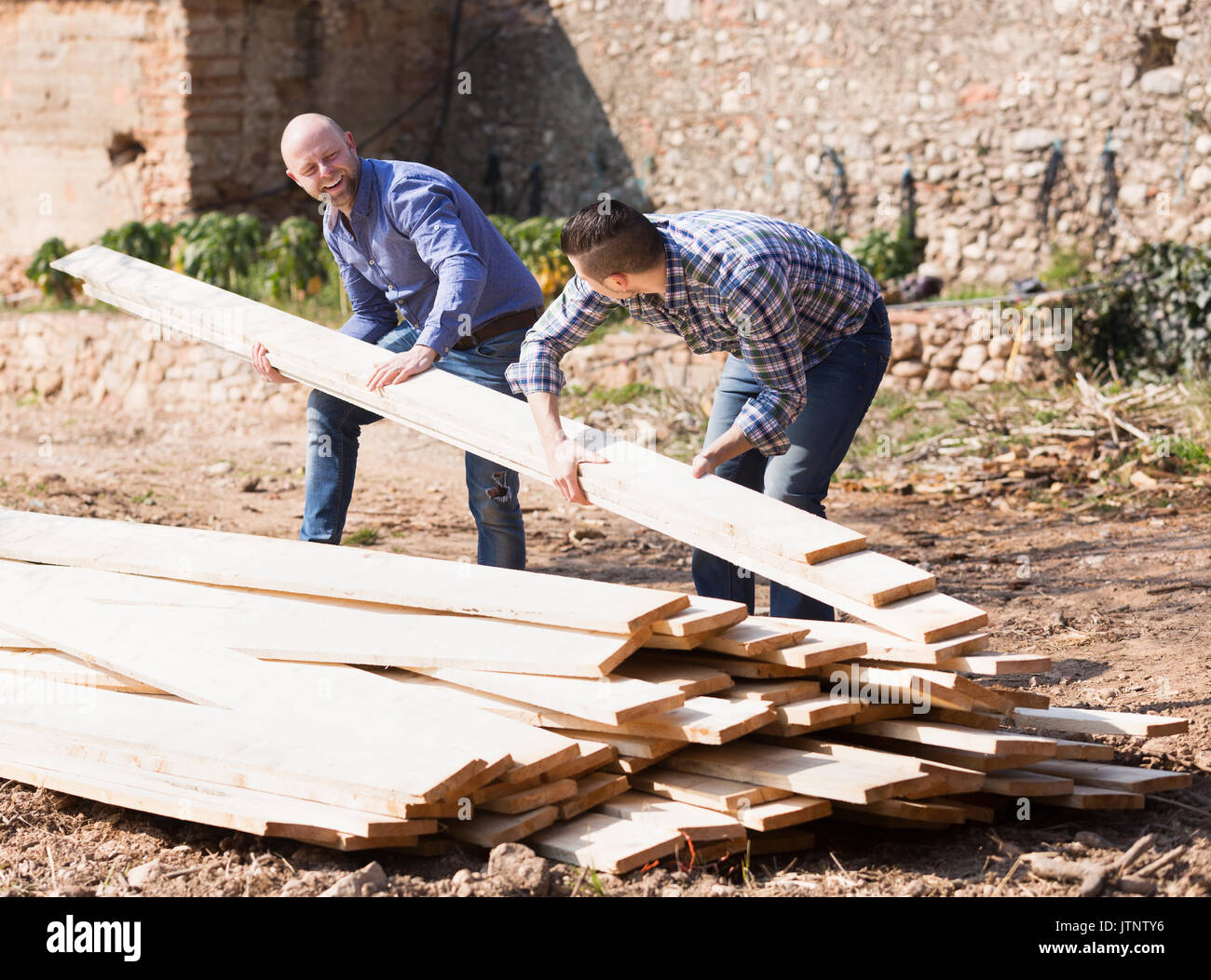 Two smiling male builders carrying over plane boards at site Stock ...