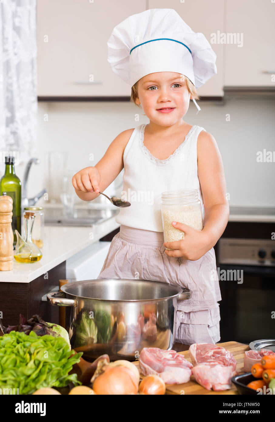 Happy cute little girl cooking with meat at home kitchen Stock Photo ...
