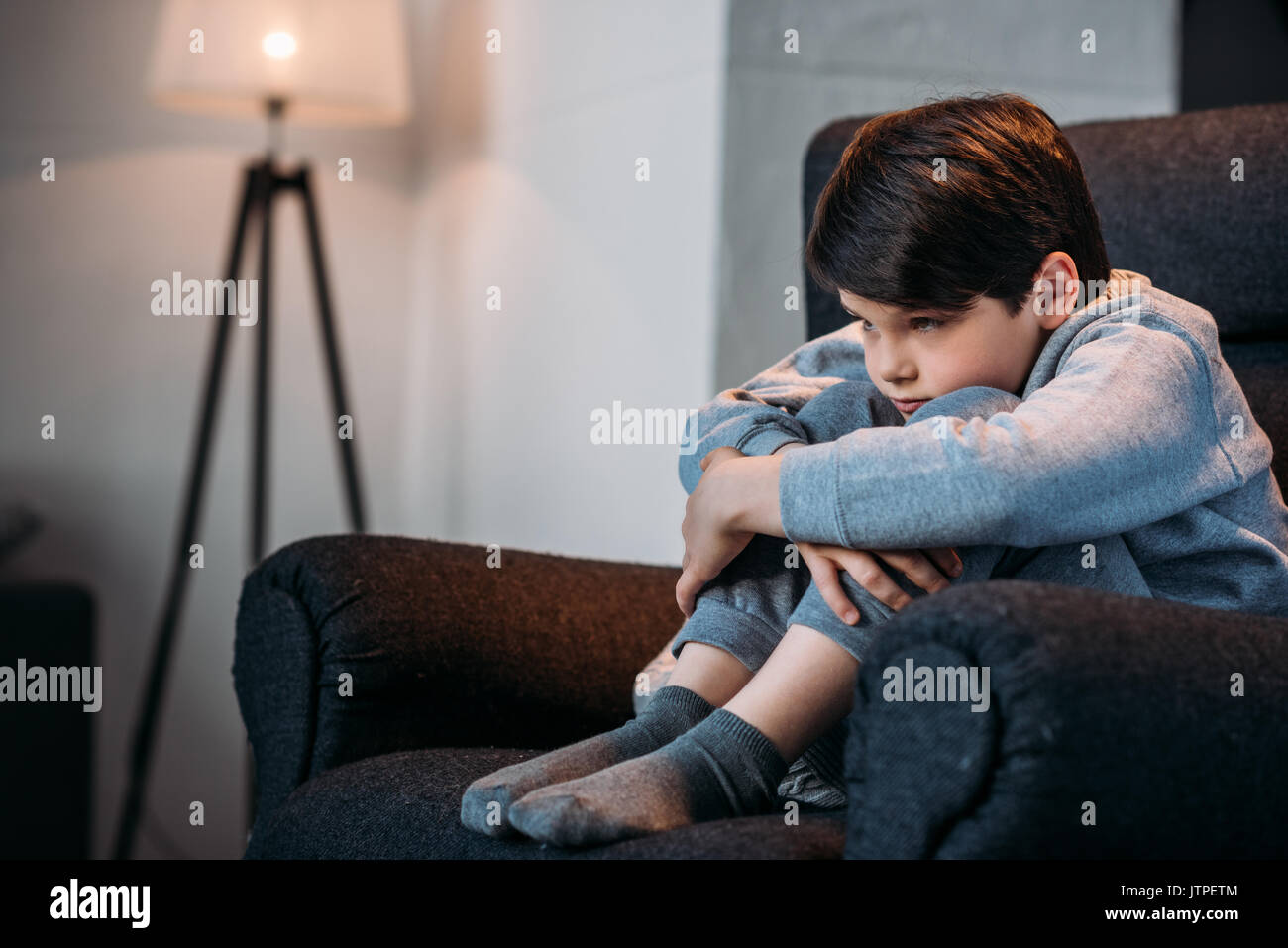 little upset thoughtful boy sitting in armchair and looking away at ...