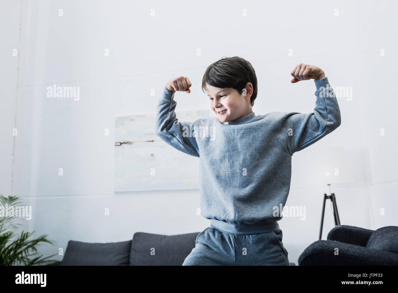 Smiling little boy showing biceps and having fun at home Stock Photo ...