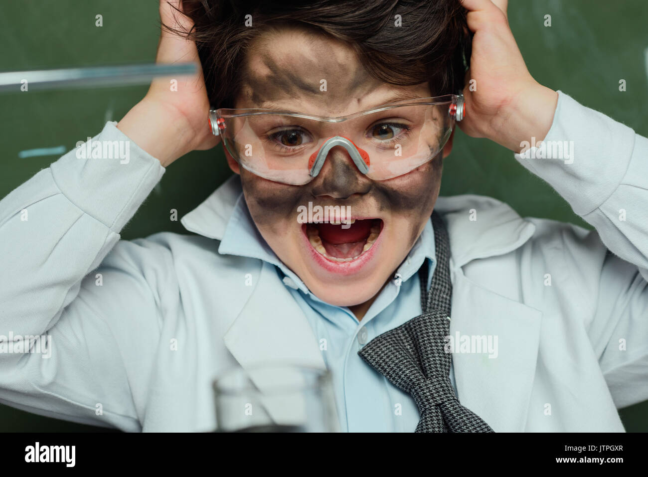 shocked boy in white coat and protective glasses after experiment in ...