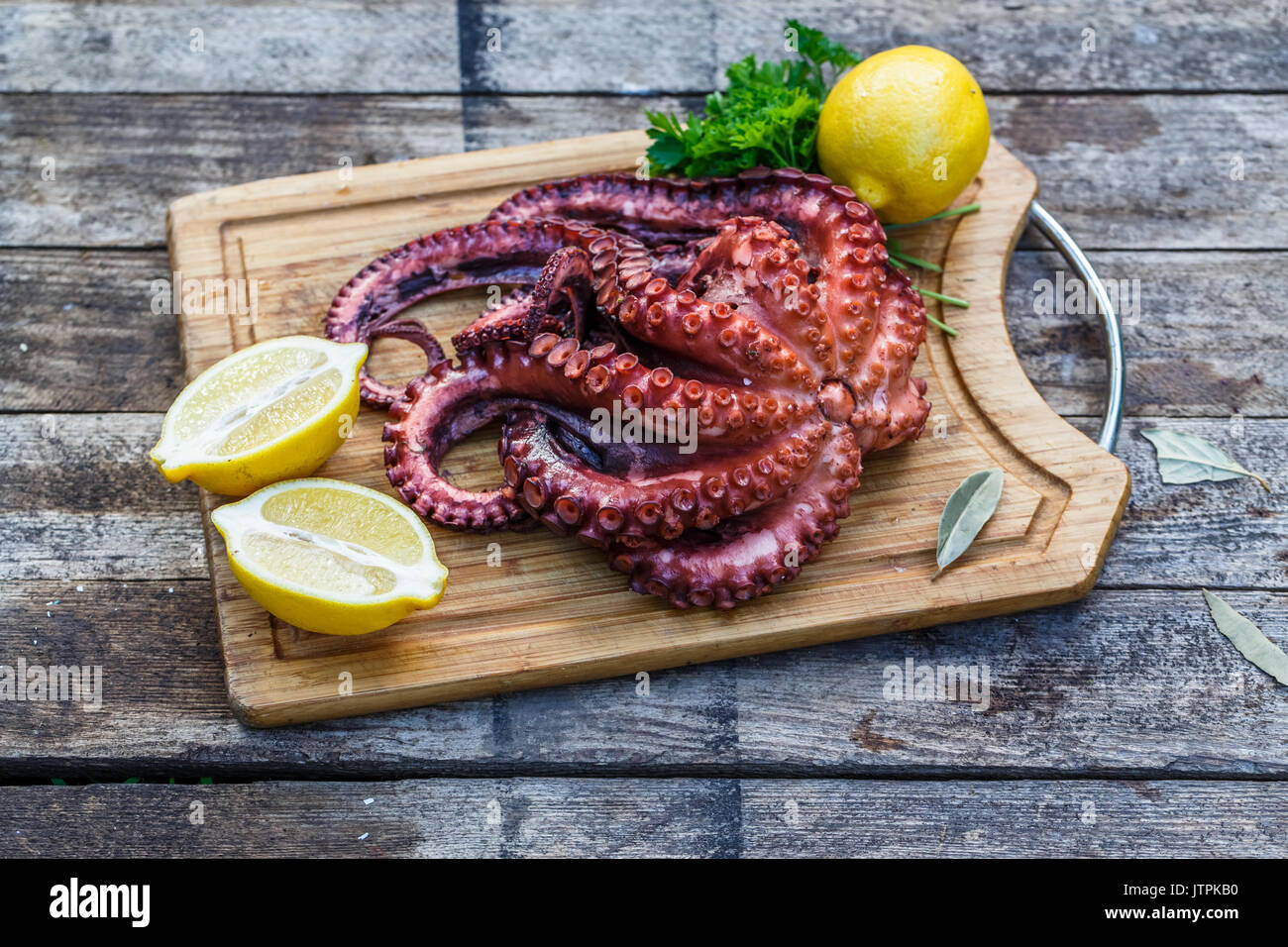 Boiled octopus ready for serve with lemon and parsley on wooden board ...
