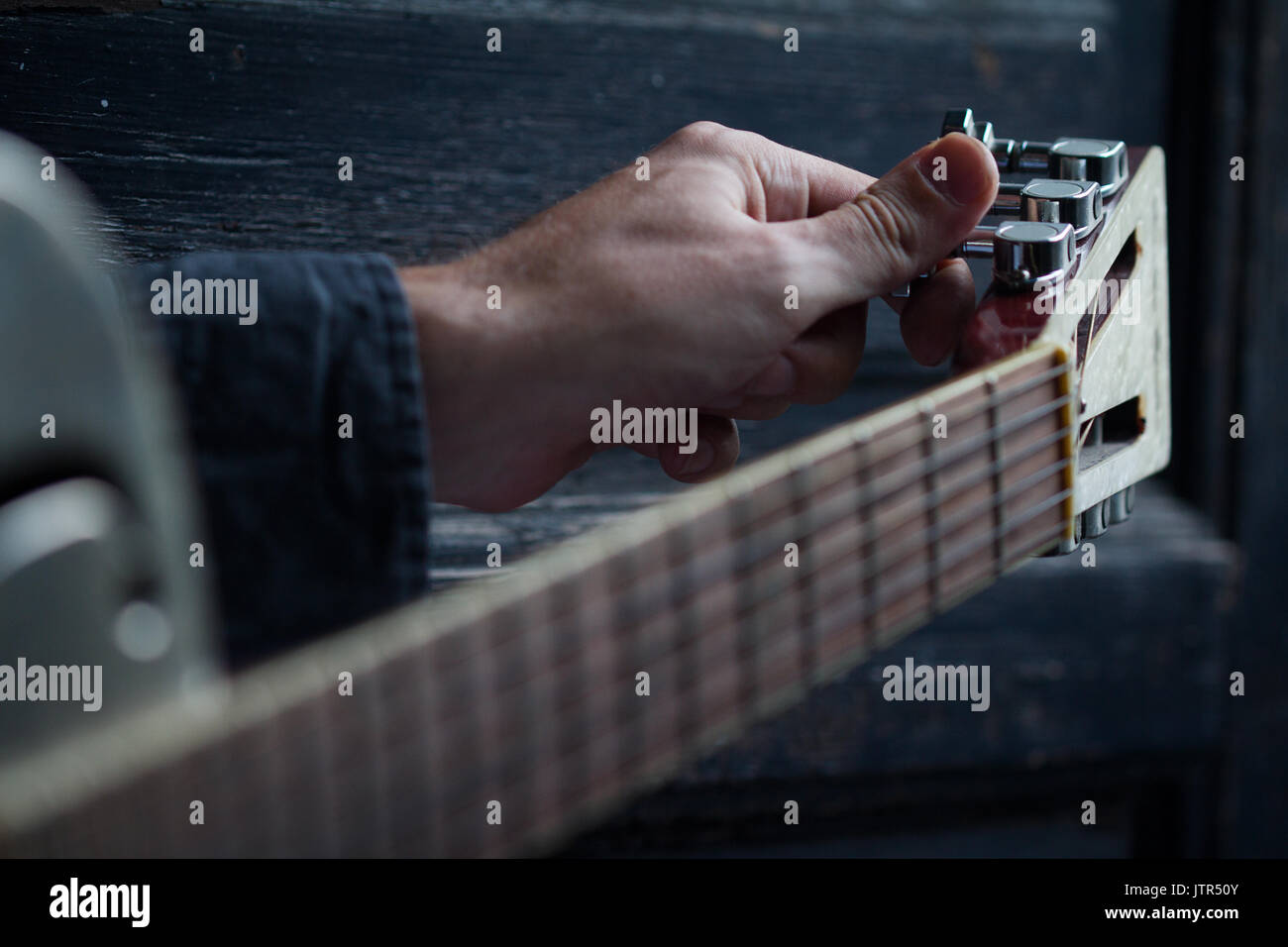 Caucasian male hand tuning an acoustic guitar on black dark wooden ...