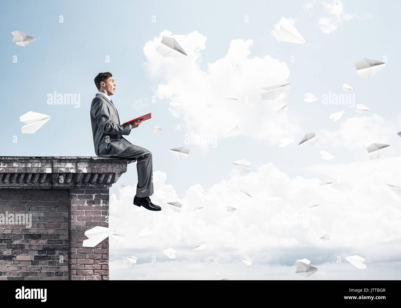 Man on roof edge reading book and cityscape at background Stock Photo ...