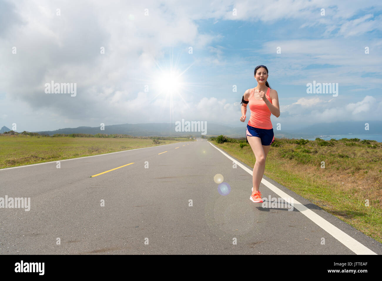 beautiful female athlete running on asphalt road and listen to music ...