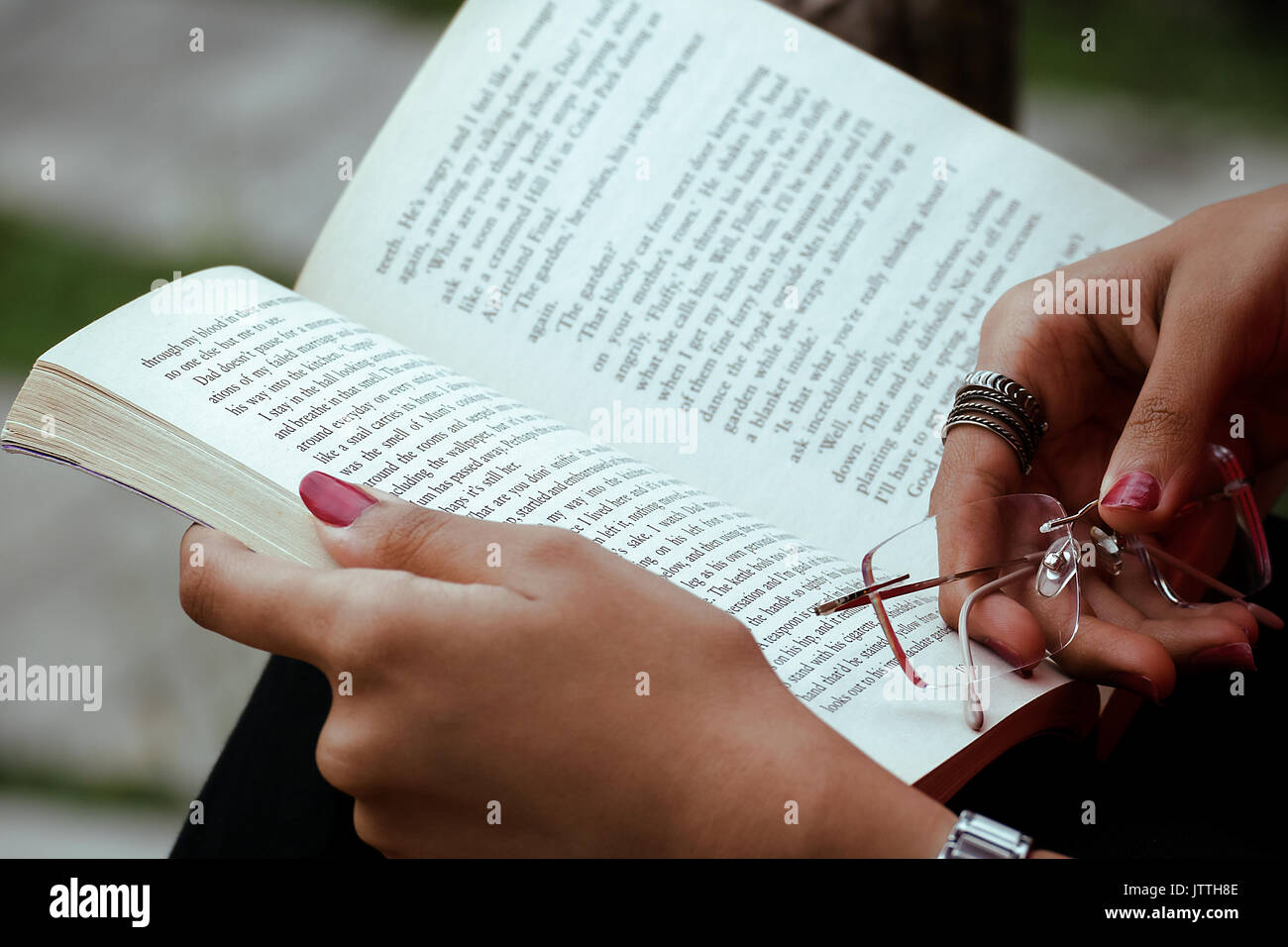 Closeup of an open book, female hands, folded spectacles in hand ...