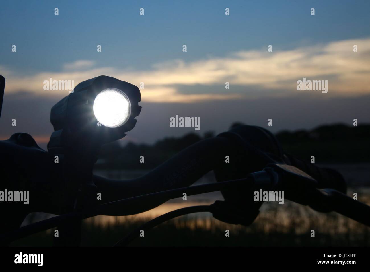 Illuminated White Bicycle Light on Handlebars at Sunset in front of ...