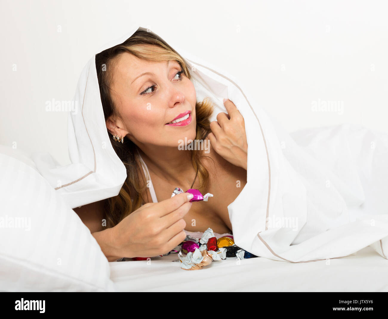 Funny woman hiding with chocolate candy under blanket Stock Photo - Alamy