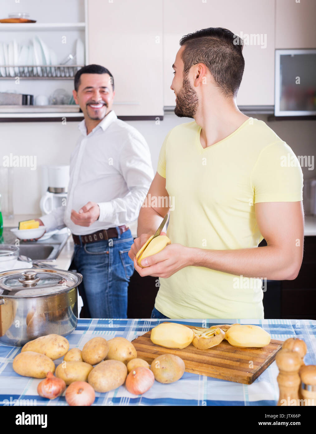 Adult son helping happy father to prepare vegetable stew at kitchen ...