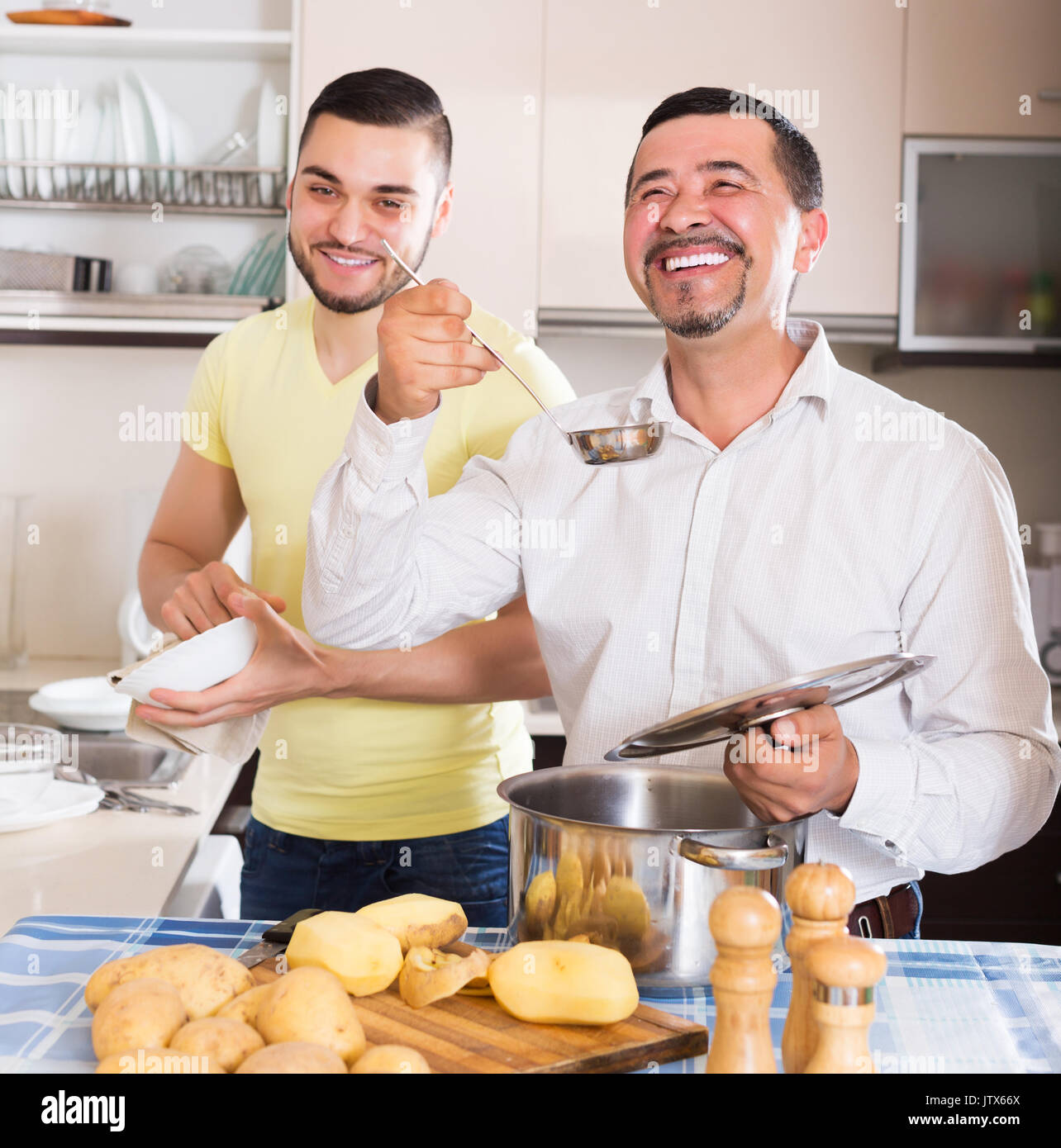 Smiling adult son helping happy father to prepare vegetable stew at ...