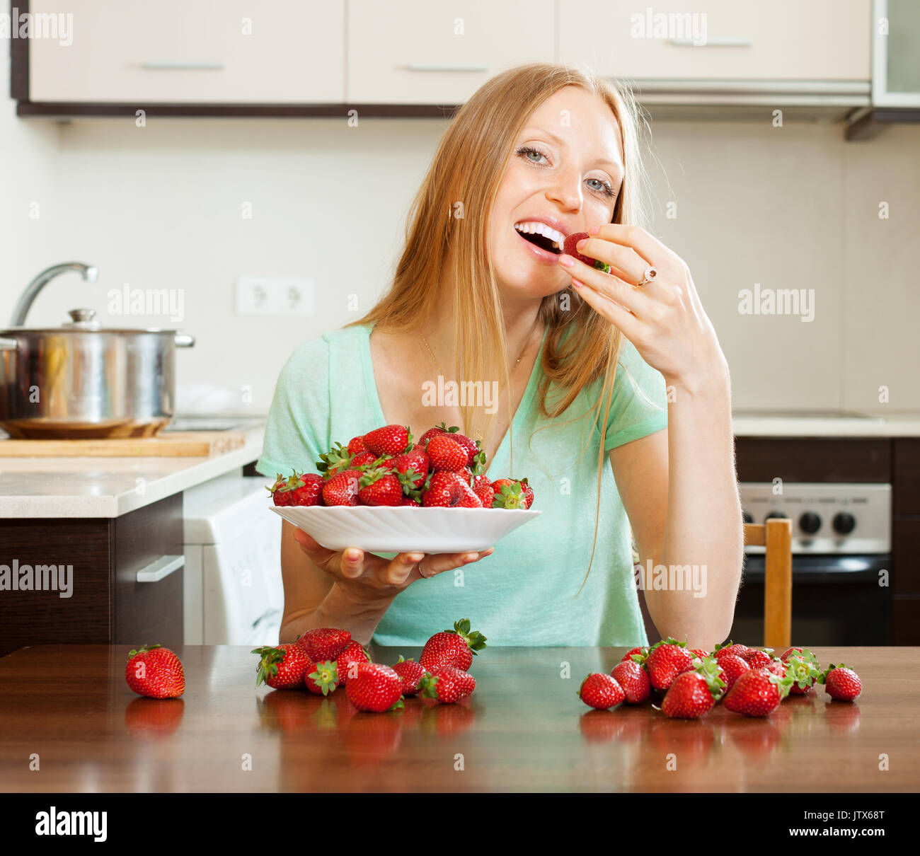 long-haired woman eating strawberry in home Stock Photo - Alamy