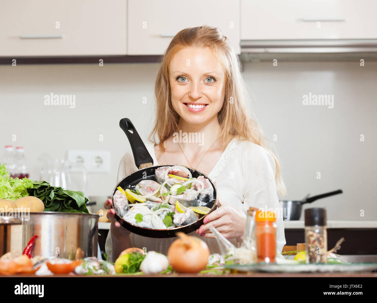 Cheeful woman cooking fish in frying pan at kitchen Stock Photo - Alamy