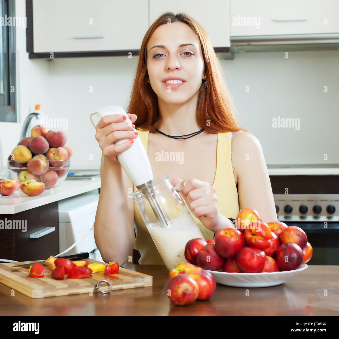 long-haired woman cooking dairy beverages with nectarines at kitchen ...