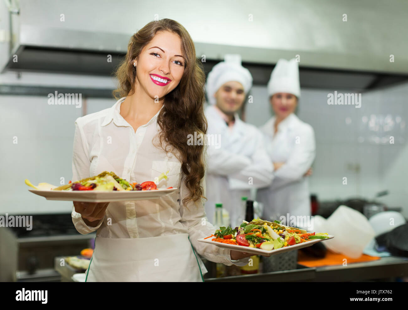 Positive waitress take plates with prepared meal at kitchen Stock Photo ...