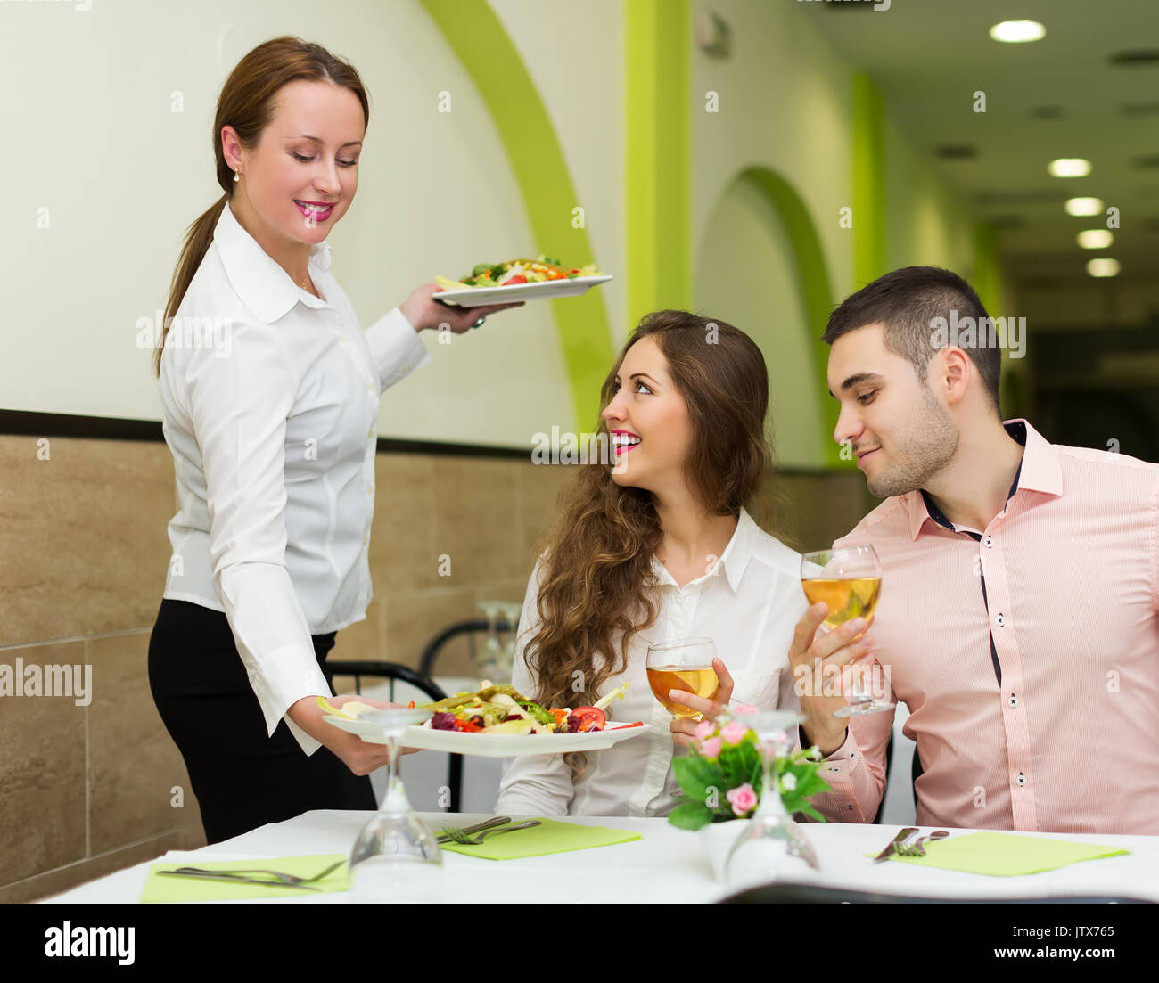 Smiling waitress brings dishes with prepared food to clients table ...