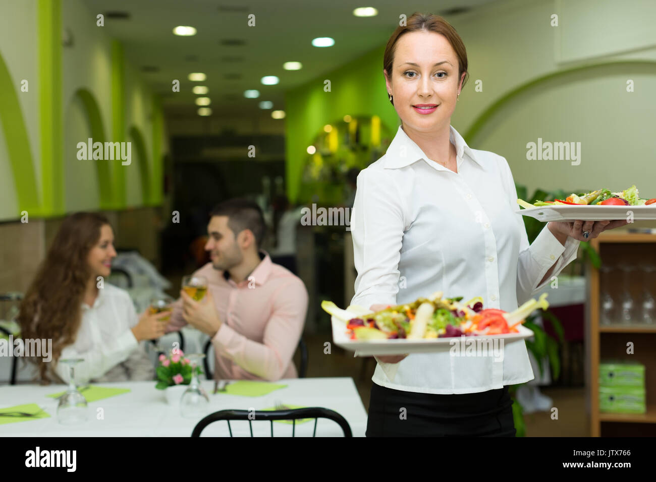 Female waiter with plates in hands serving guests table in cafe Stock ...