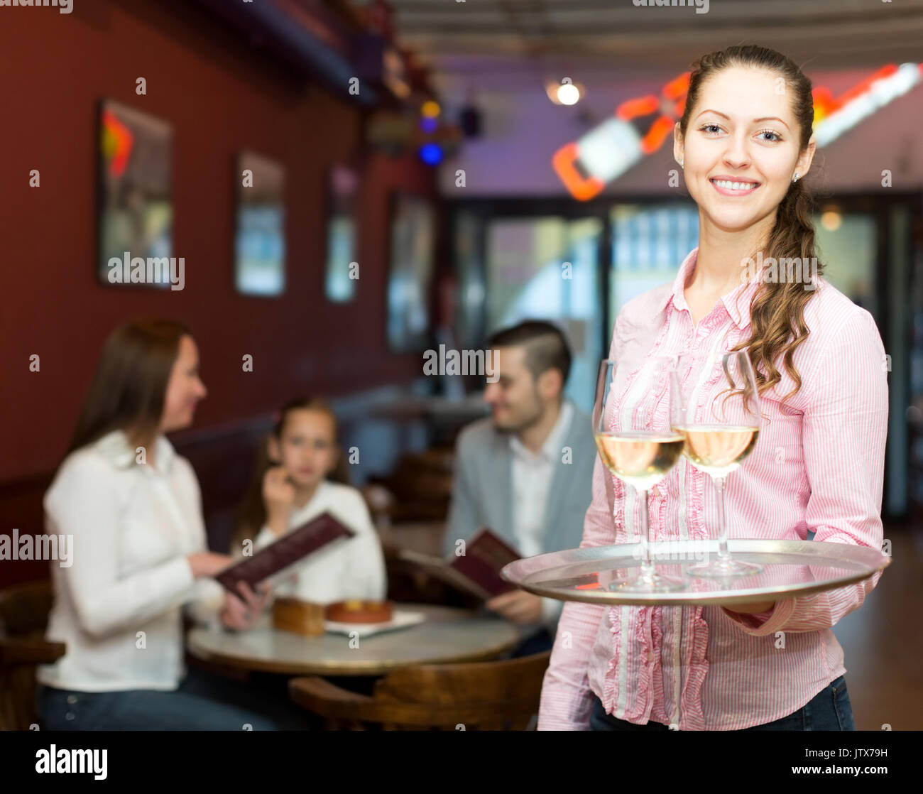 Smiling waitress and cheerful family with young daughter reading menu ...