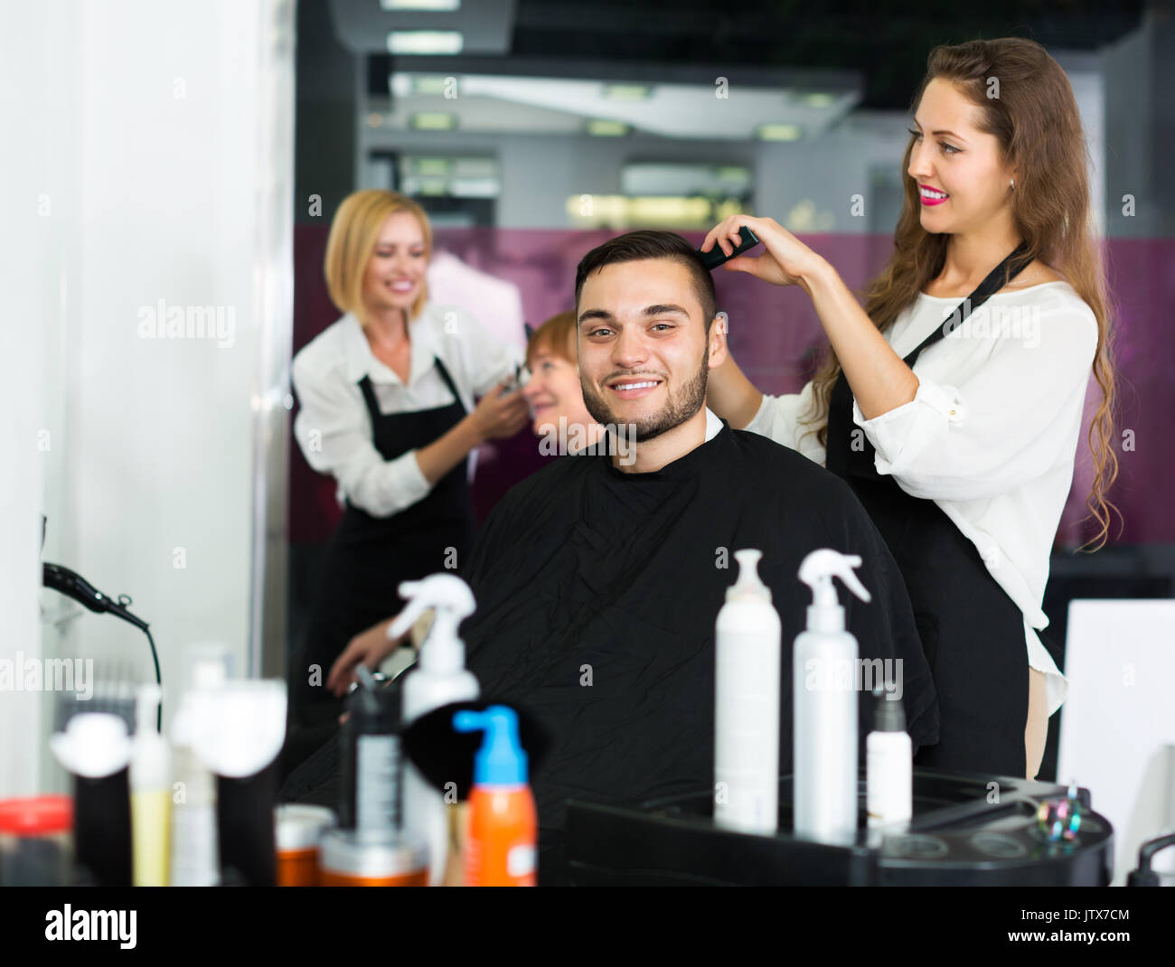 Positive professional adult woman hairdresser doing hairstyle for young ...