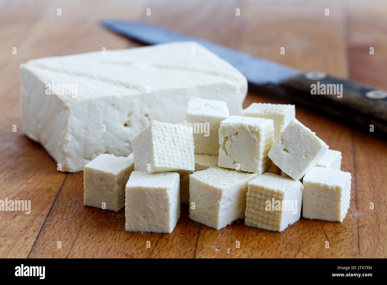 Single block of white tofu with cut tofu cubes and rustic knife on ...