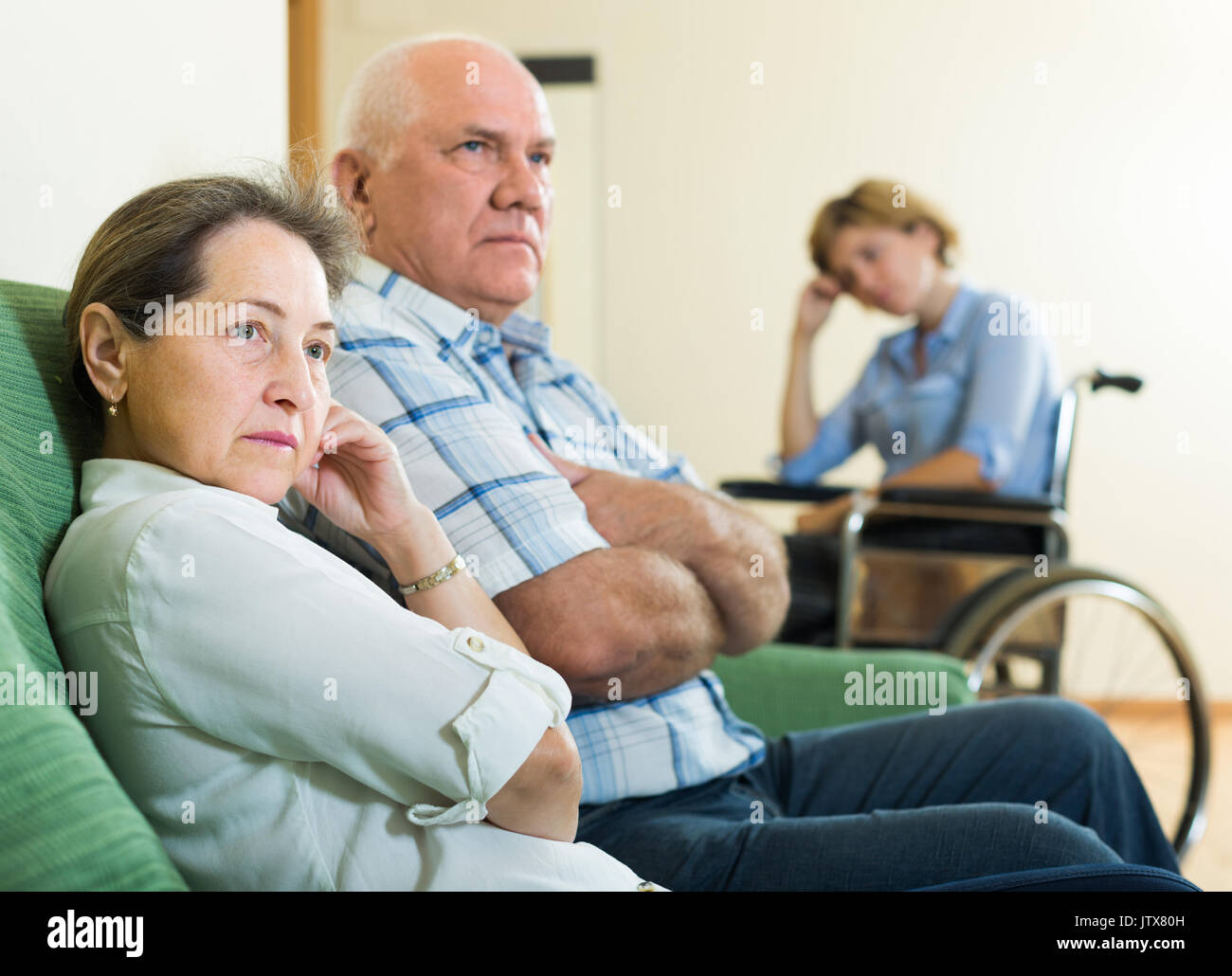 Tired elderly couple and disabled person on chair indoor. Focus on ...