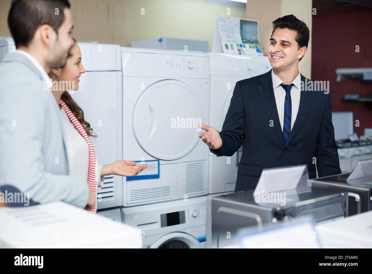 Positive salesman and adult buyers in store of domestic appliances ...