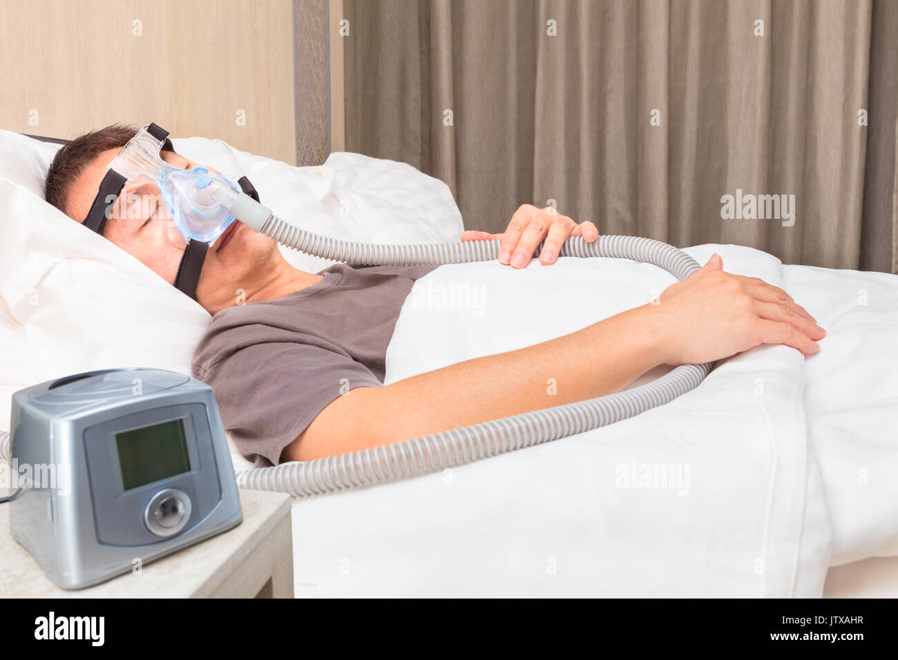 middle age asian man sleeping in his bed wearing CPAP mask connecting ...