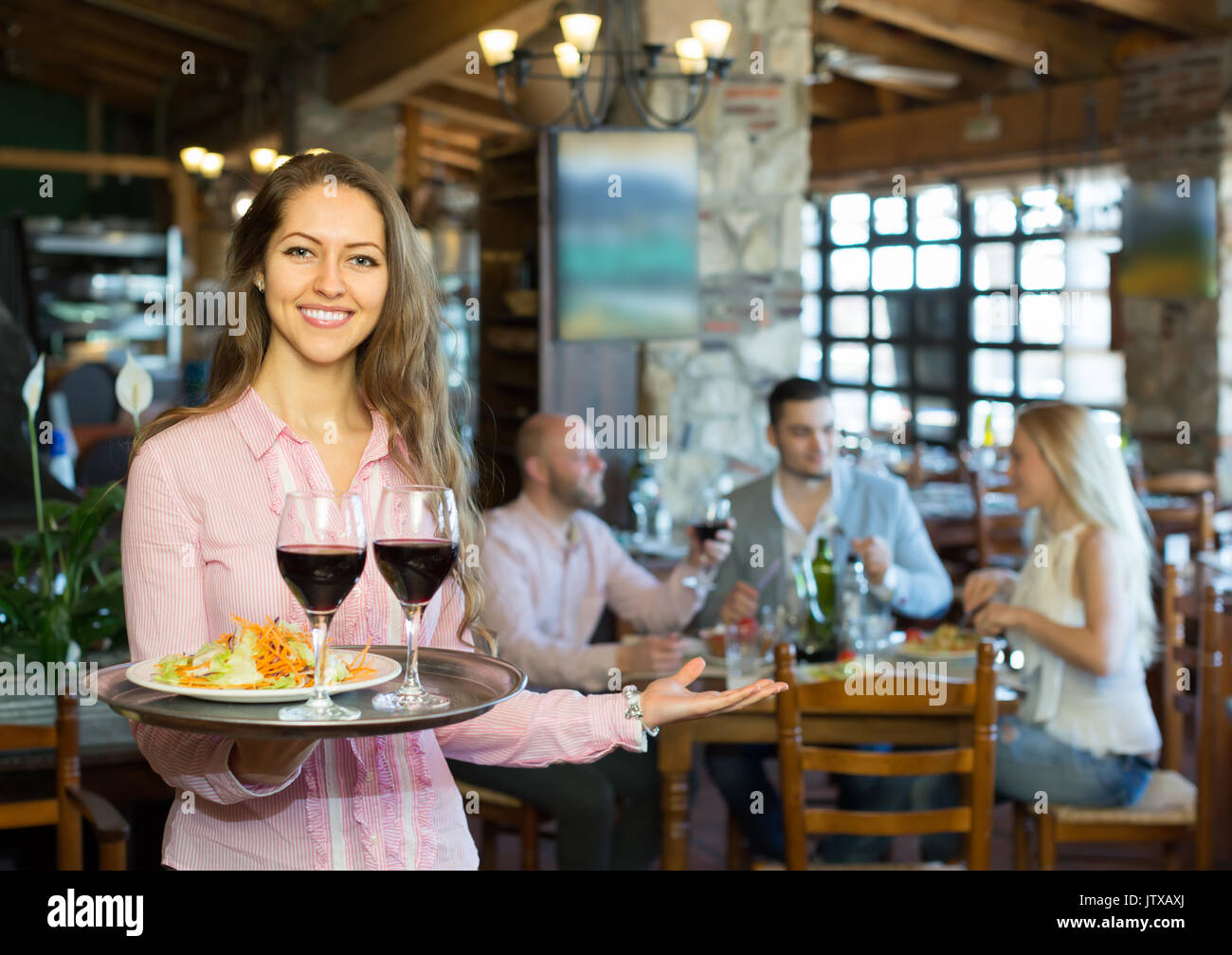 Cheerful young female waiter serving restaurant guests at table Stock ...