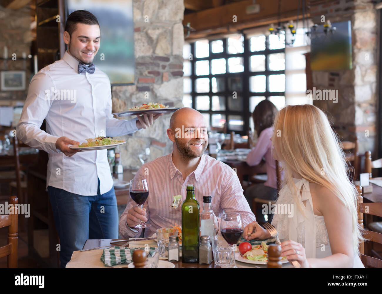 Happy smiling male waiter serving restaurant guests at table. Selective ...