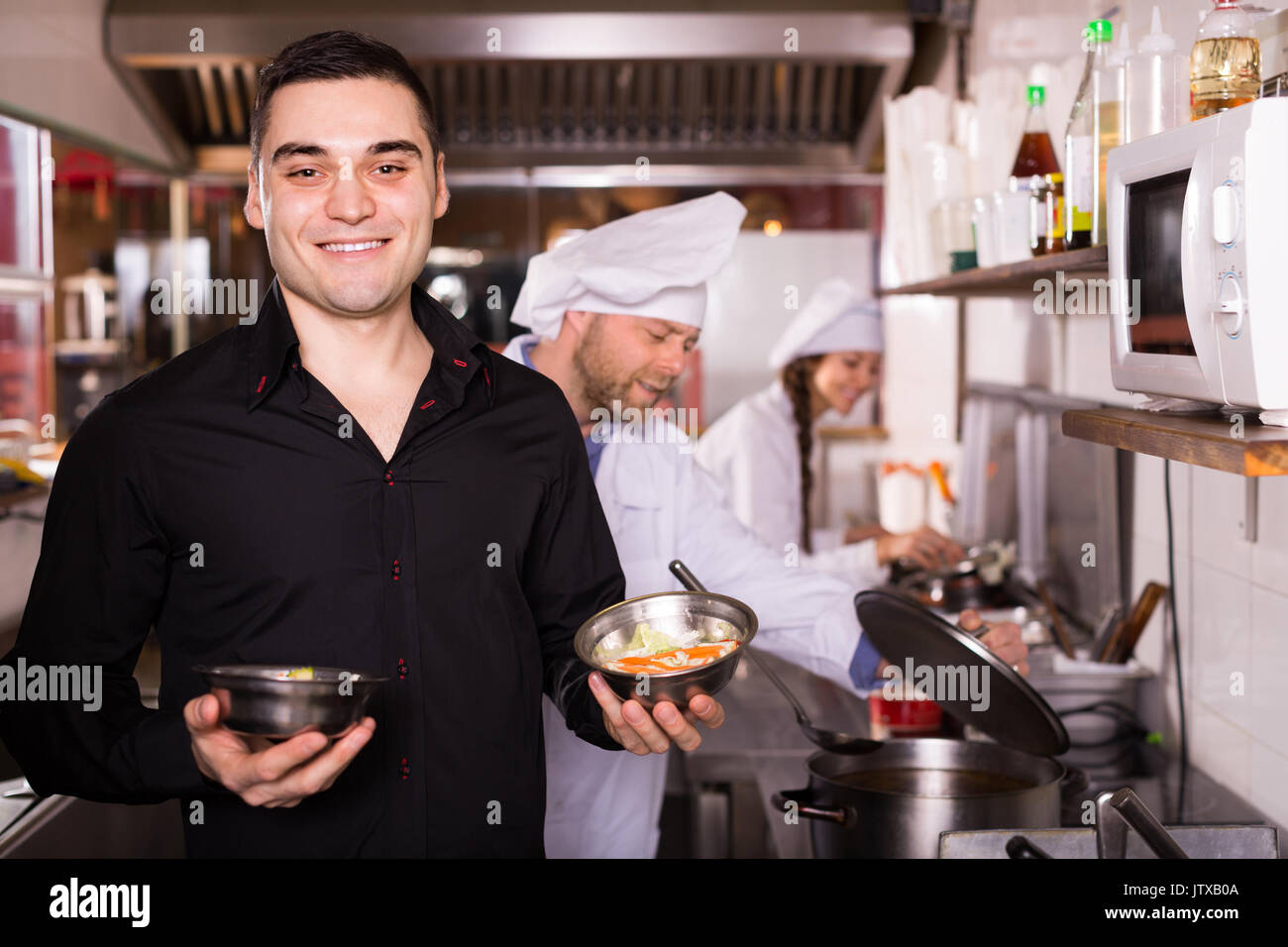 Portrait of happy male waiter holding dishes and cooks at fastfood ...