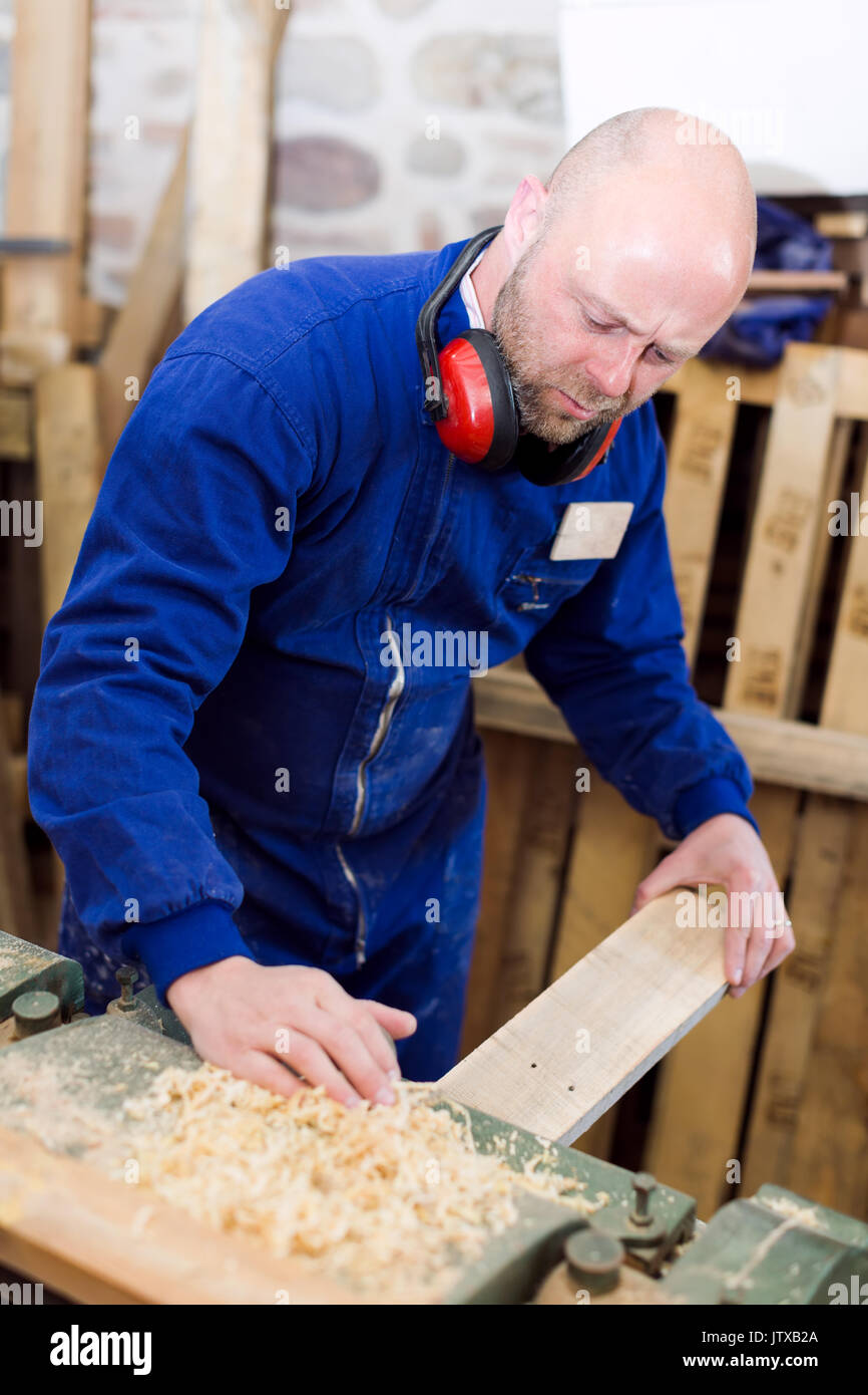 Concentrated carpenter wearing a blue robe and red protective ear muffs ...