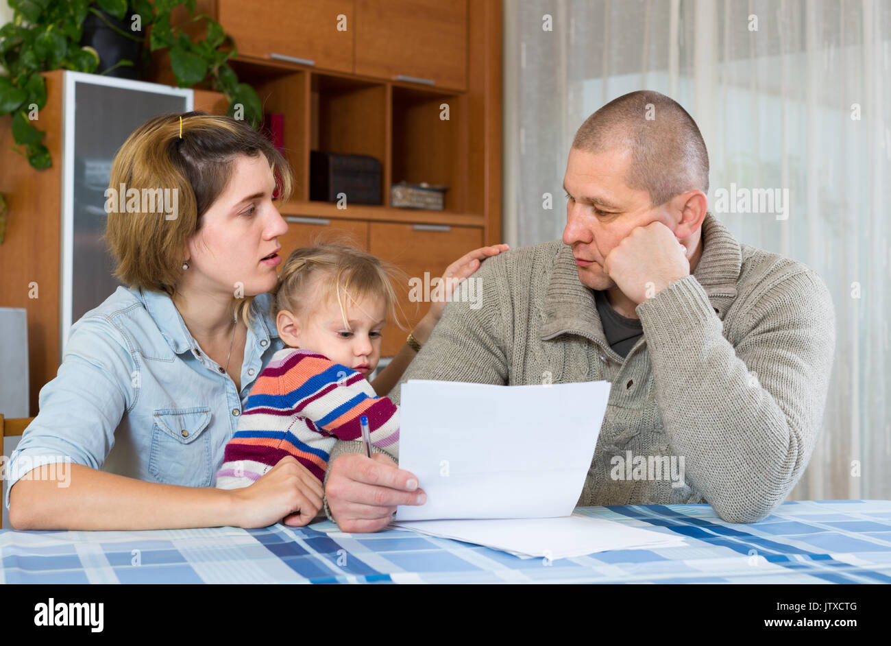 Worried family with child sitting with financial documents at home ...