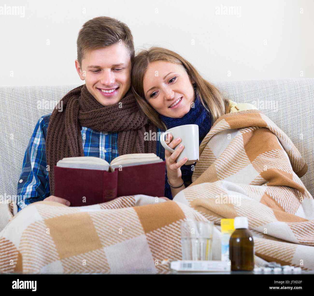 Frozen couple sitting on couch under blanket with book Stock Photo - Alamy