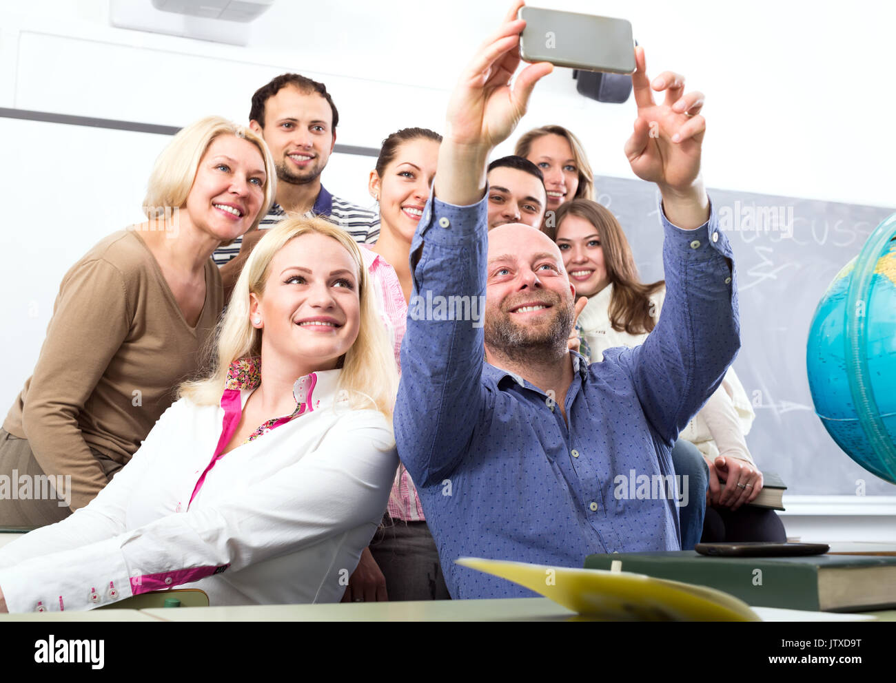 Smiling students posing in a classroom while their lecturer is taking a ...