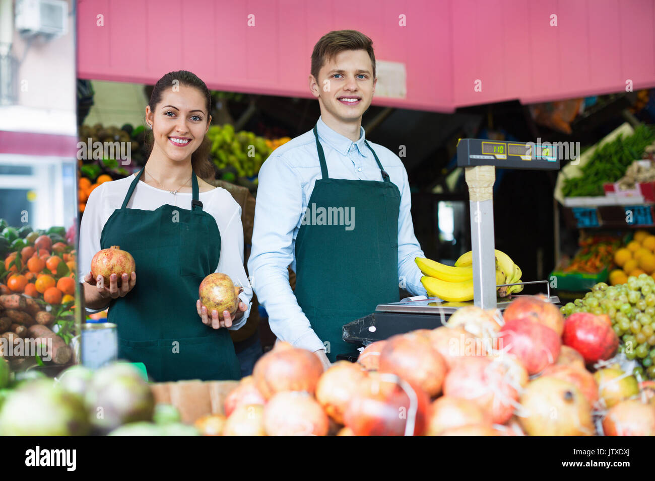 Young smiling positive sellers having vegetables and fruits on displays ...