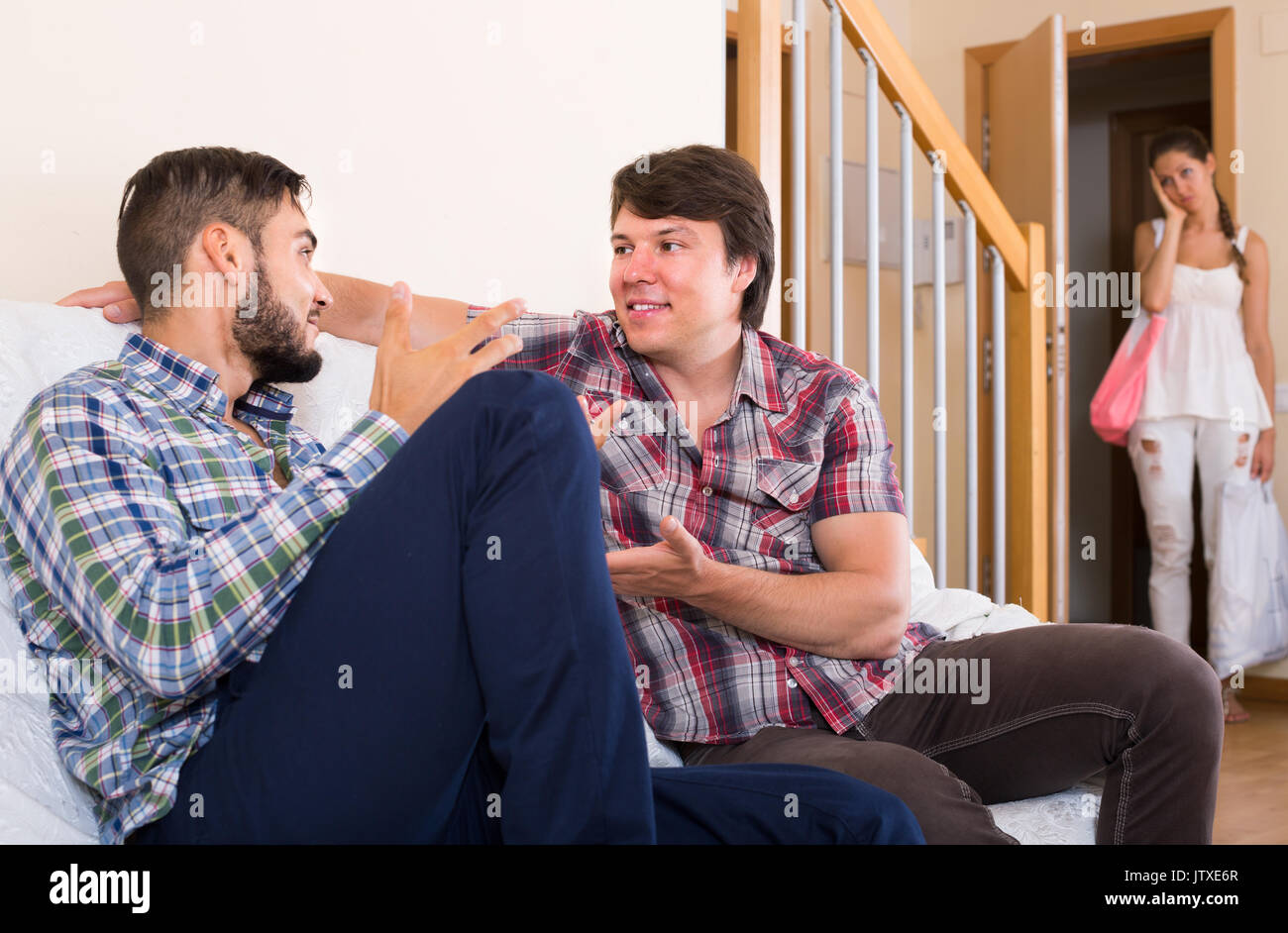 Suspicious wife looking at husband flirting with male friend Stock ...