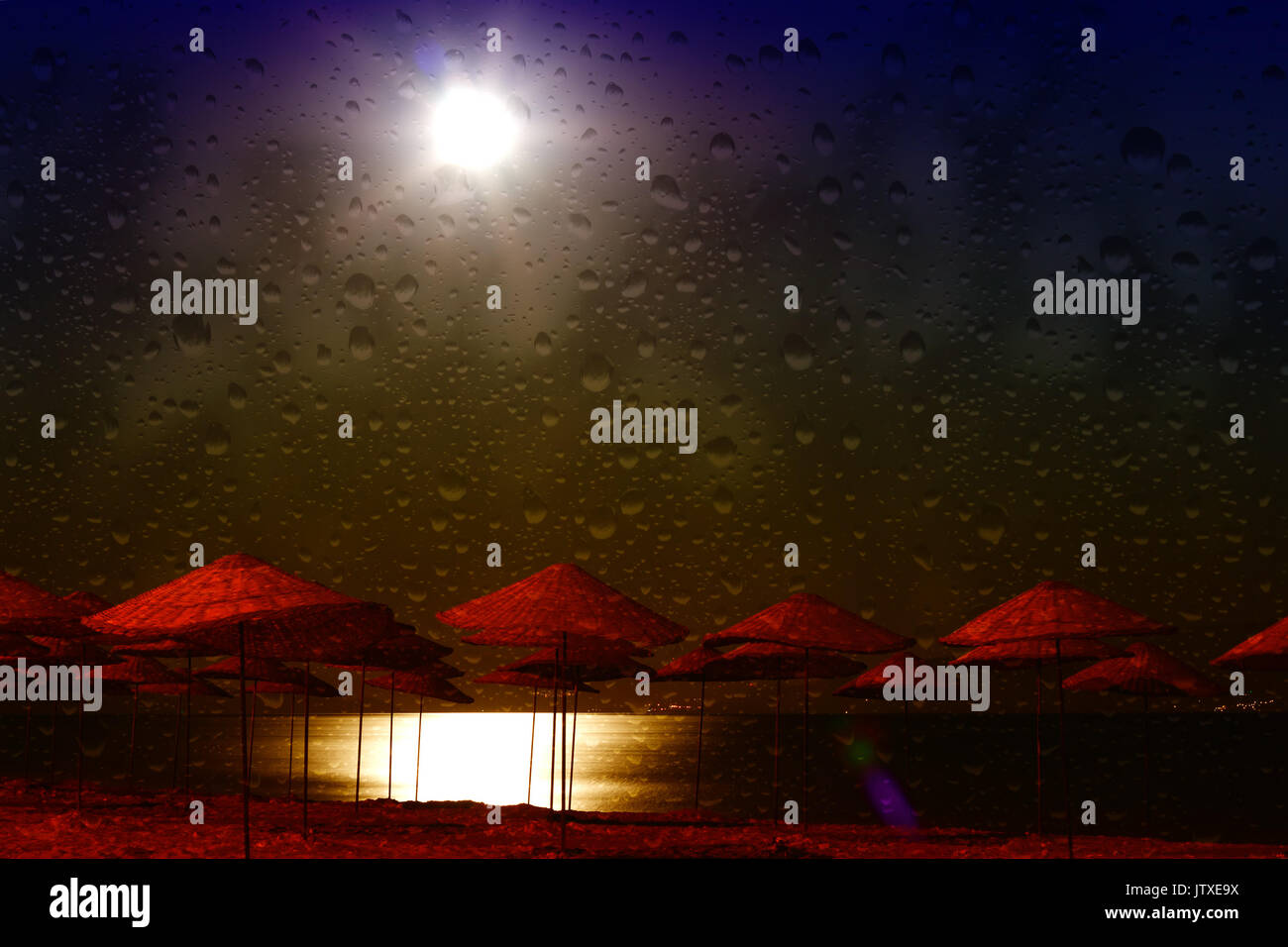 Looking through a misty window with raindrops at parasols on the beach ...