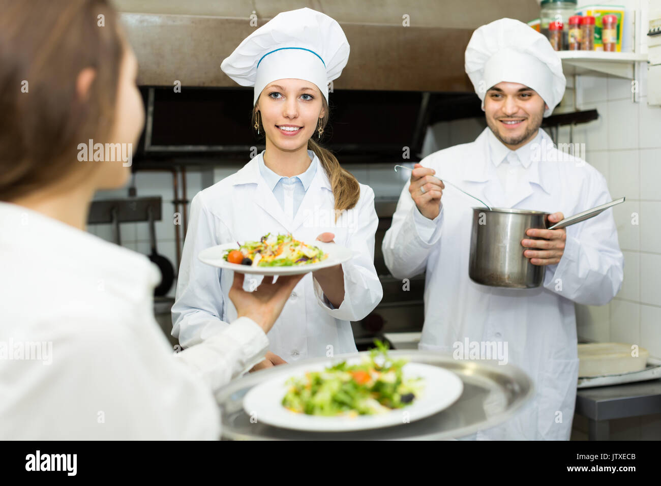 Smiling waitress taking dish from chef on restaurant kitchen. Selective ...