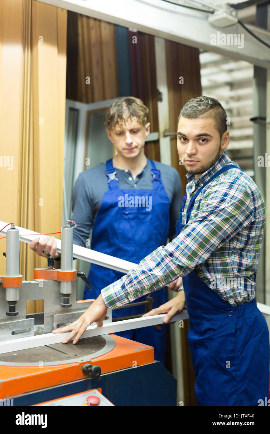 A couple of adult workers are working around the milling machine ...