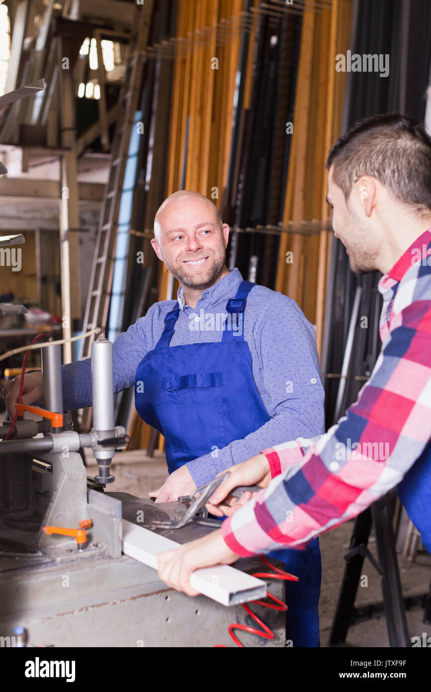Two happy workmen in uniform working on machine in PVC shop Stock Photo ...