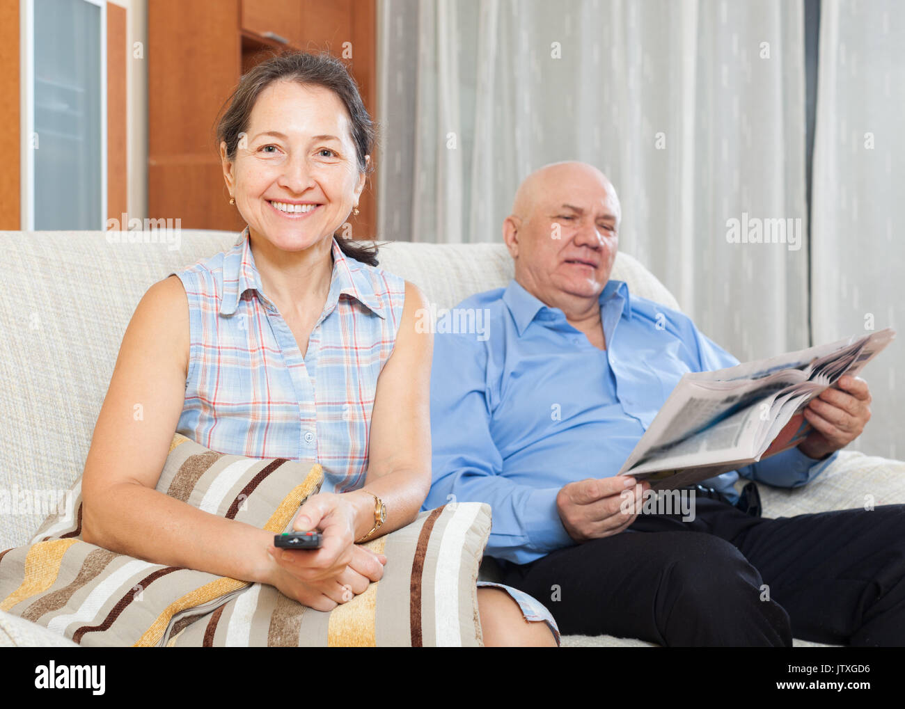 mature woman with TV remote against elderly man with newspaper in home ...