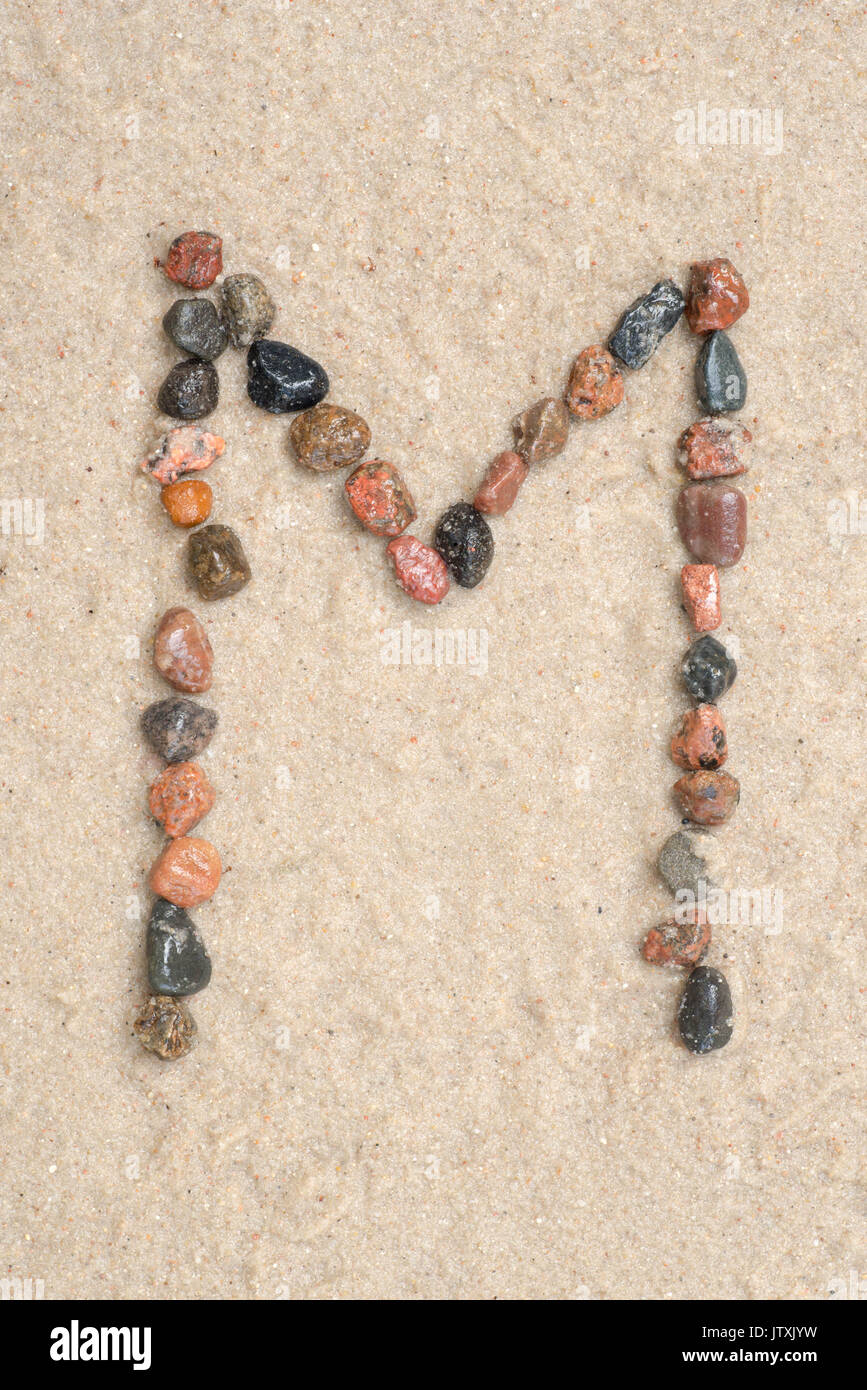 pebble m letter on sand background Stock Photo - Alamy