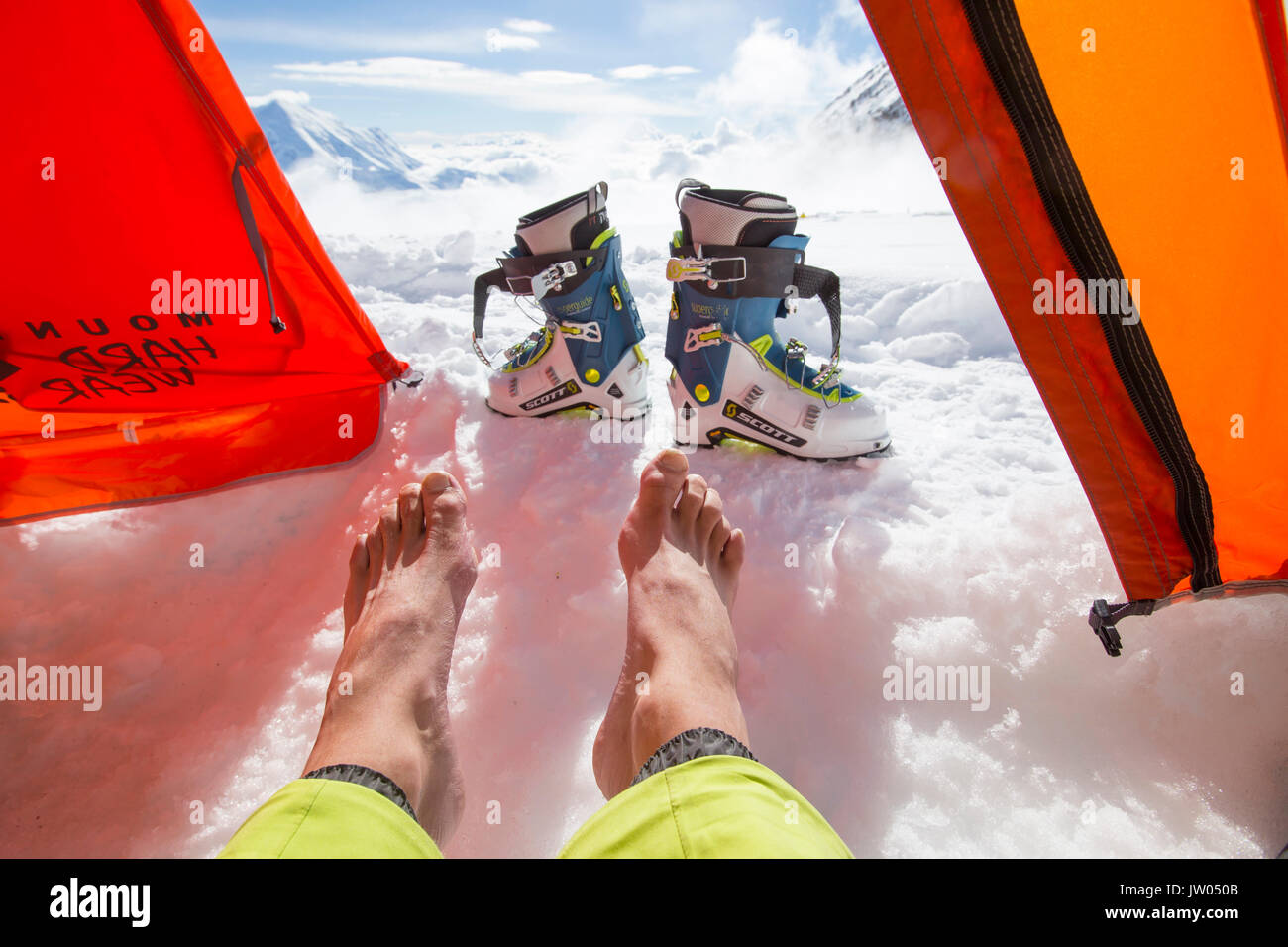 A ski mountaineer is resting his tired feet in the vestibule of a tent ...