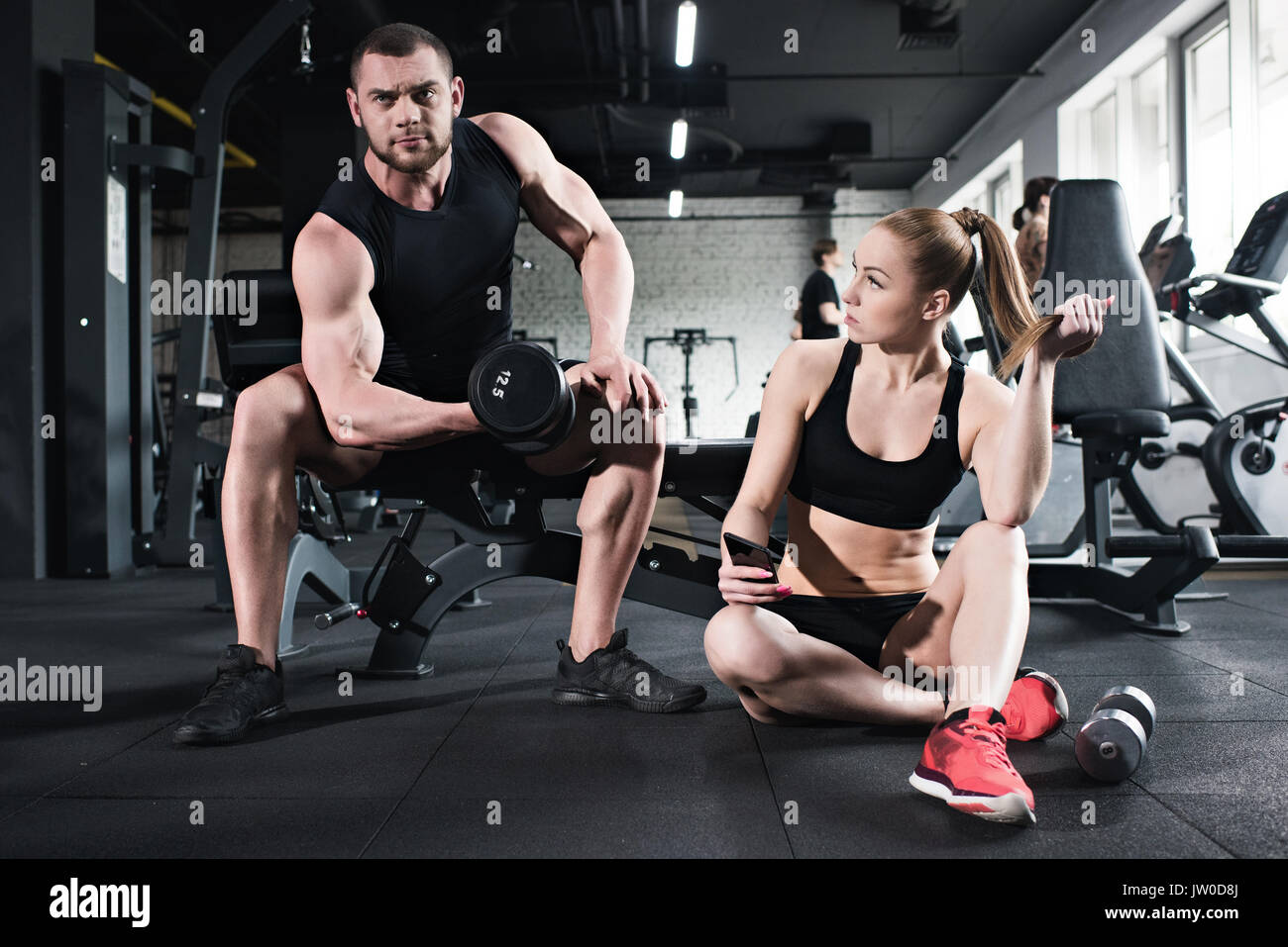 man training with dumbbell while woman holding smartphone at gym Stock ...